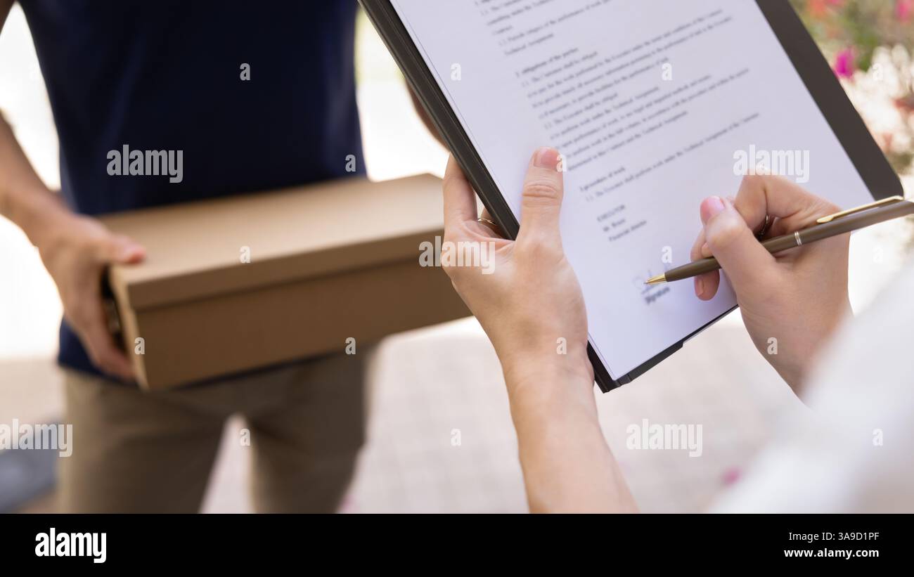 Courier holding package box while recipient signs confirmation form ...