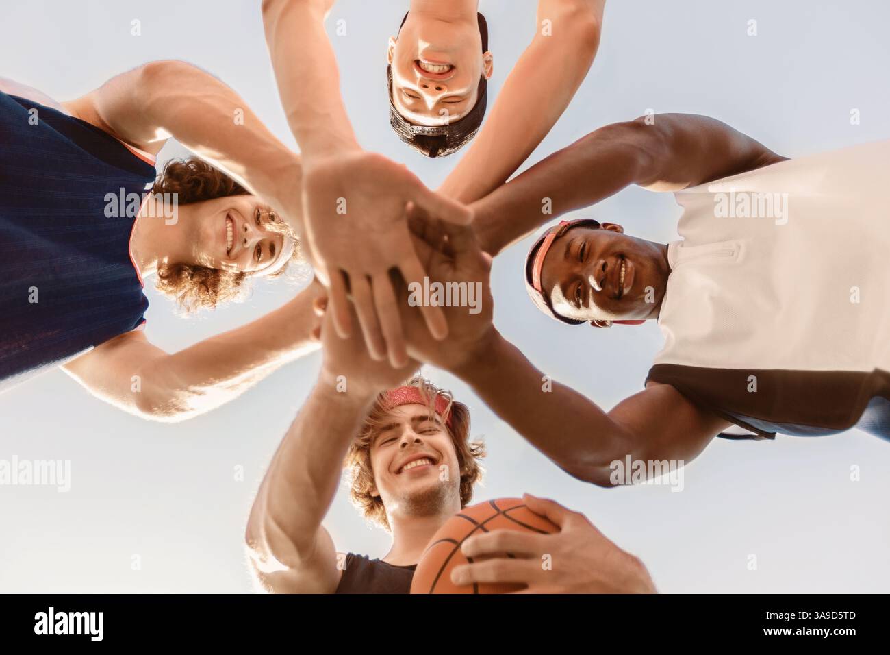 Bottom view of happy multiracial basketball team putting their hands ...