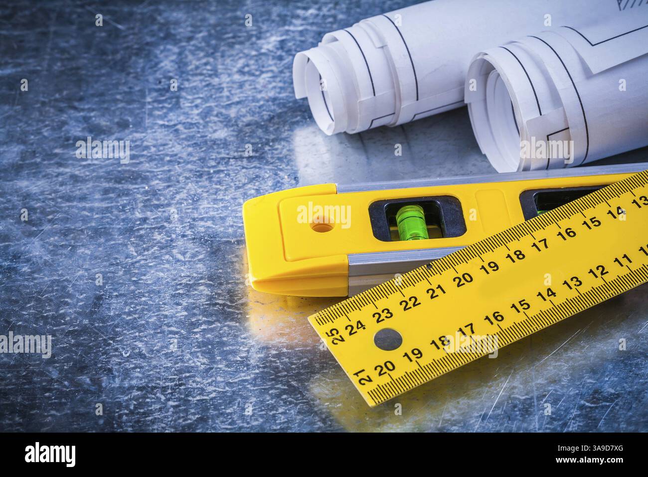 Rolled up blueprints ruler and construction level on metallic scratched ...