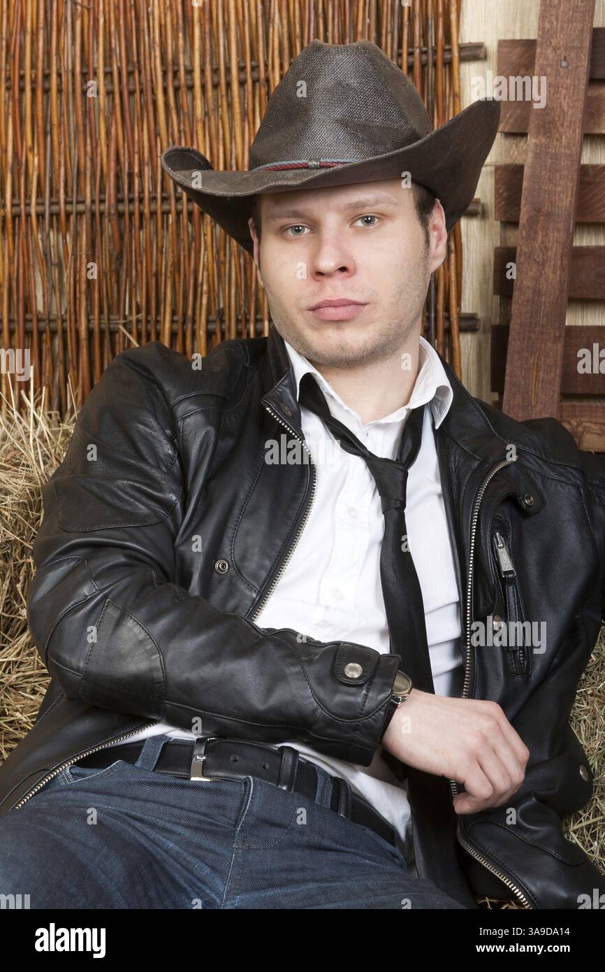 Glam cowboy in leather jacket in the rural interior is sitting on a ...