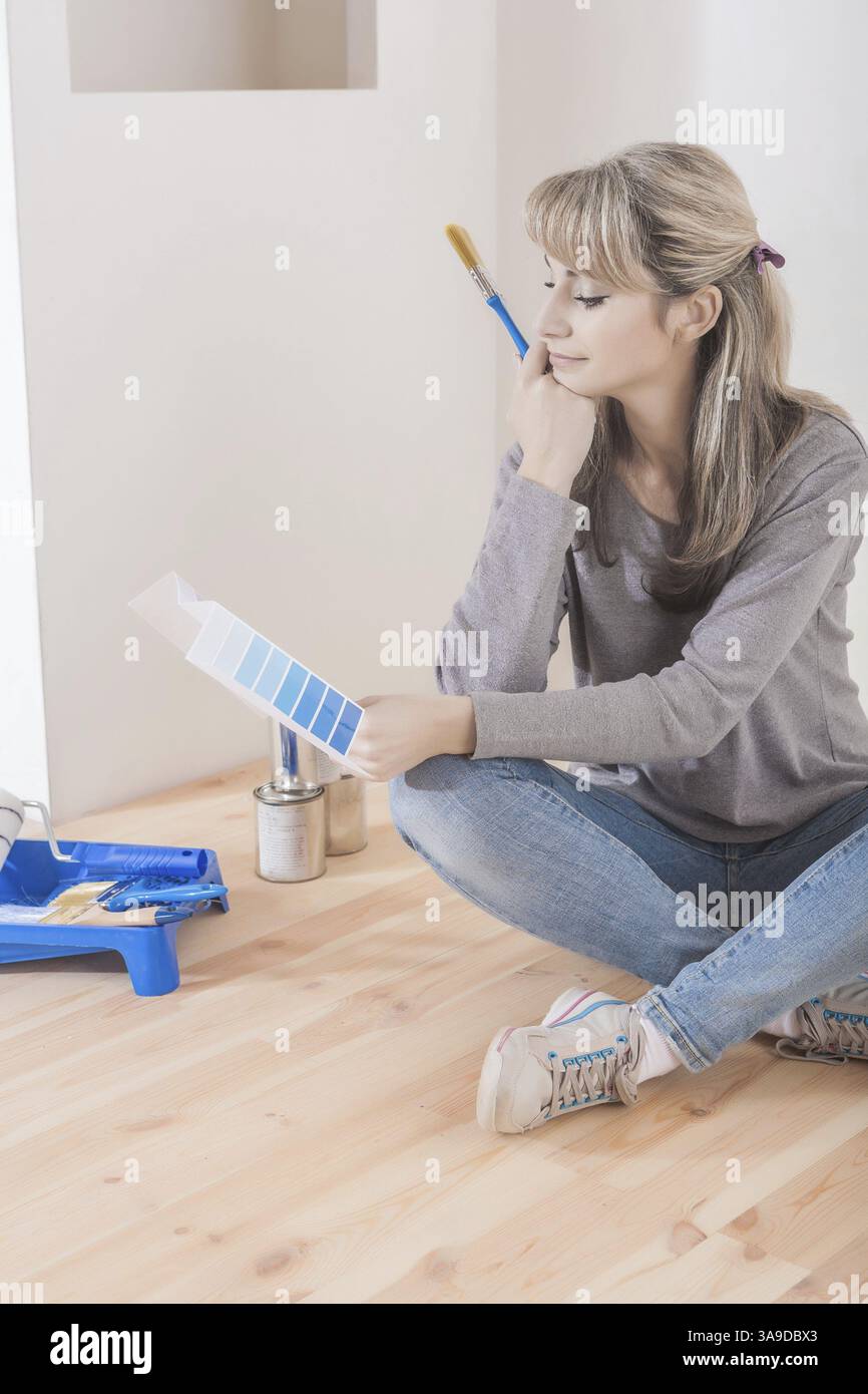 A beautiful female sitting on floor with sampler and paint brush selecting color Stock Photo - Alamy