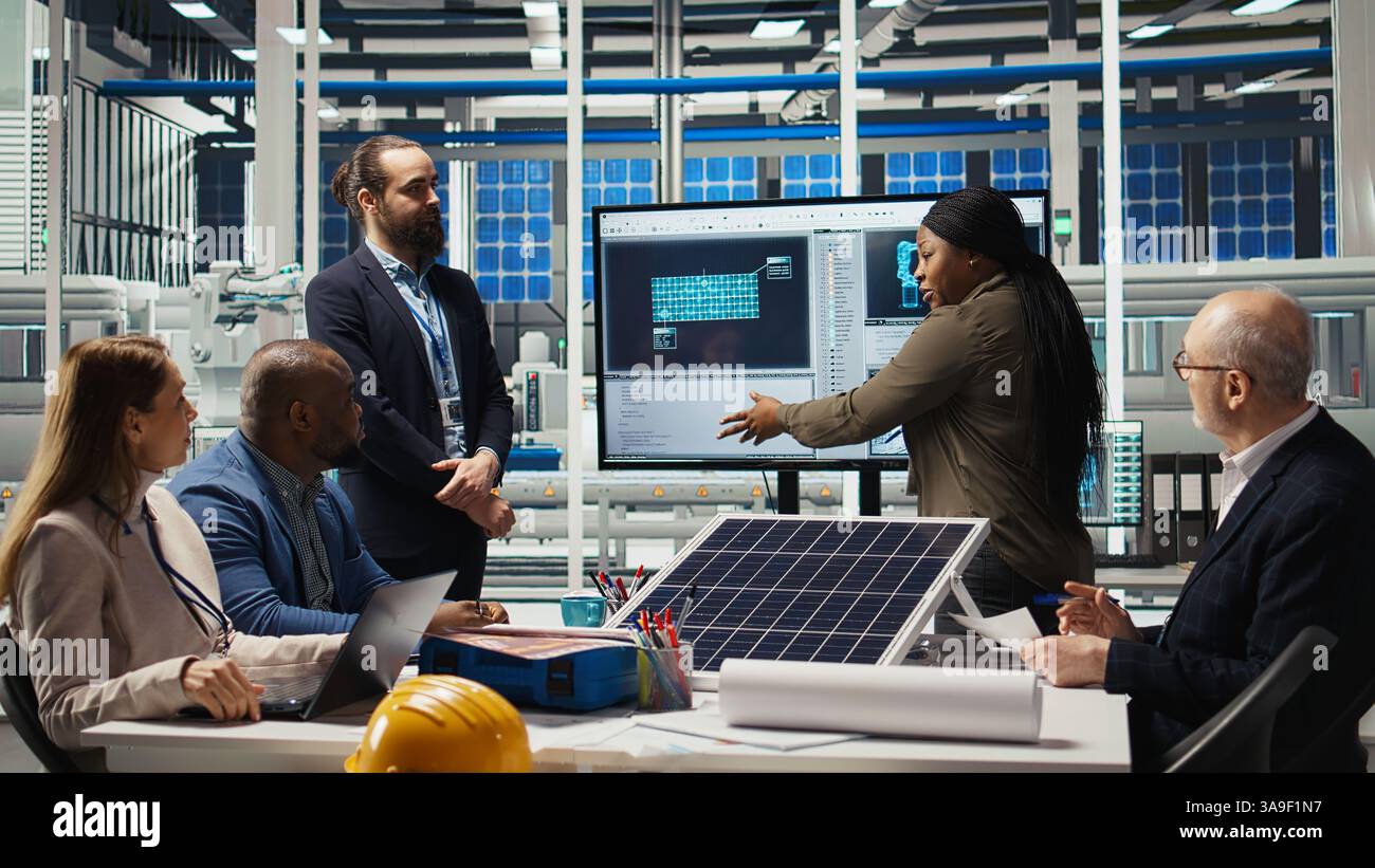 Photovoltaics plant researchers doing meeting, looking at monitor, evaluating solar cells to ...