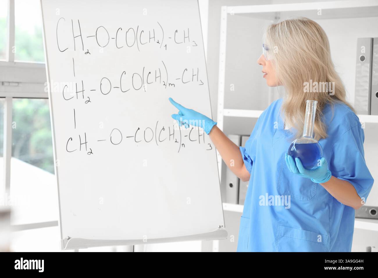 Female scientist with flask of sunflower sample writing formulas on ...
