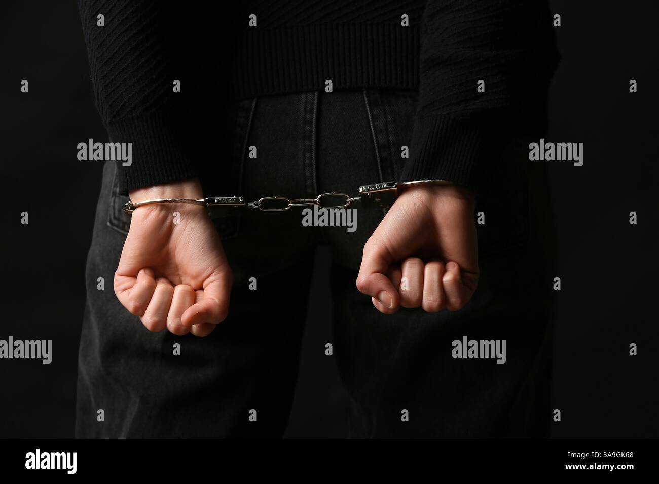 Young woman in handcuffs on black background, back view Stock Photo - Alamy
