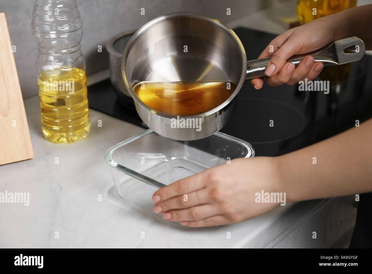 Woman pouring used cooking oil into glass container at white marble ...