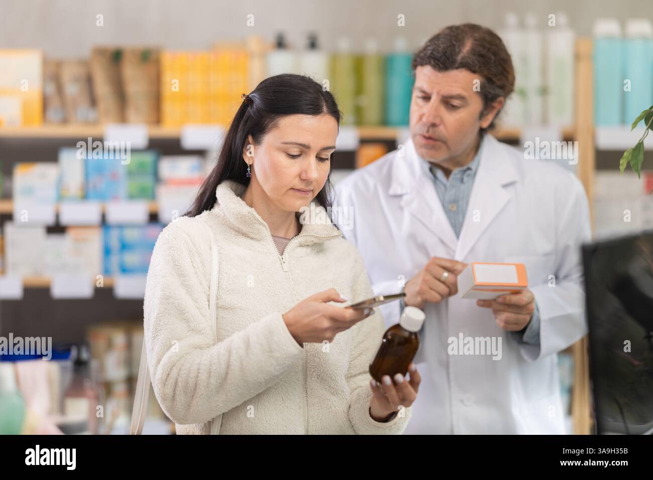 Middle-aged woman scanning QR-code on syrup while pharmacist offering ...