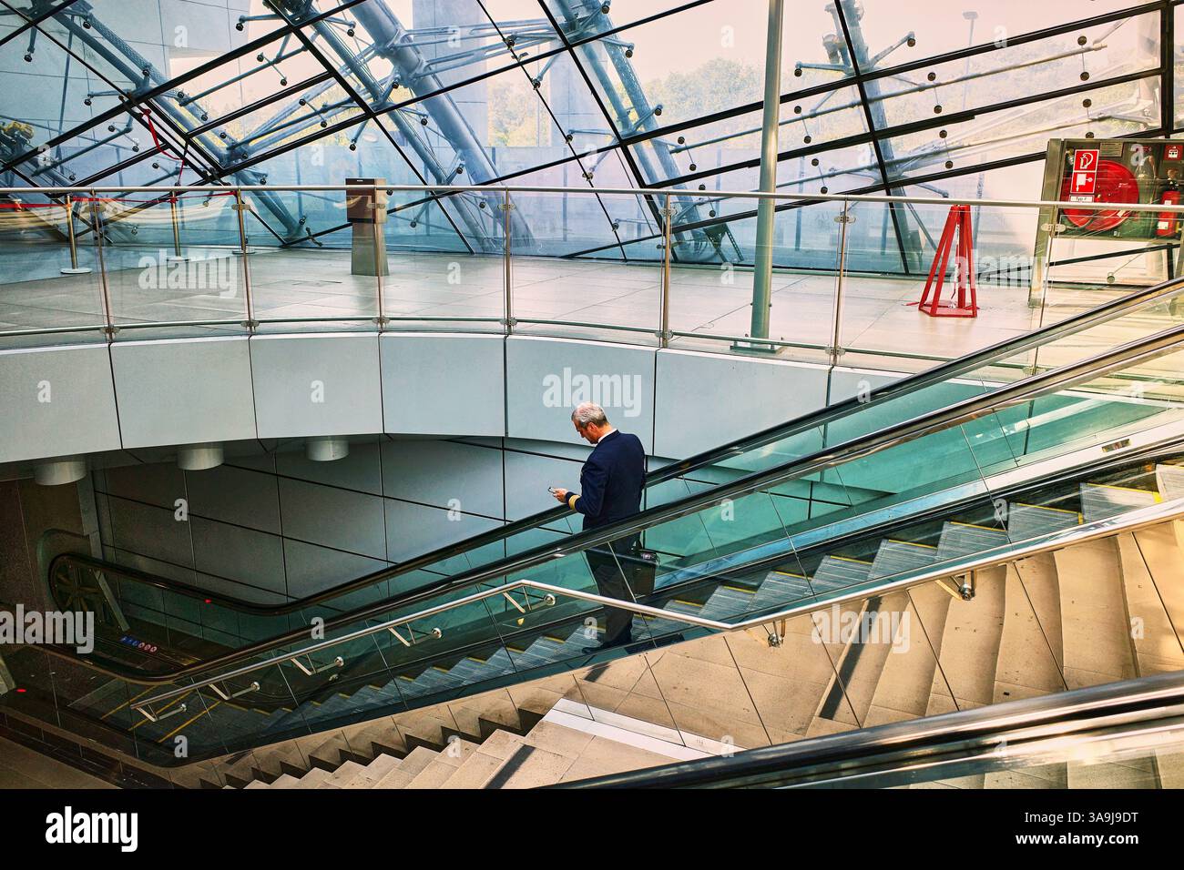 Male Airline Pilot in Uniform on escalator in an airport checks his ...