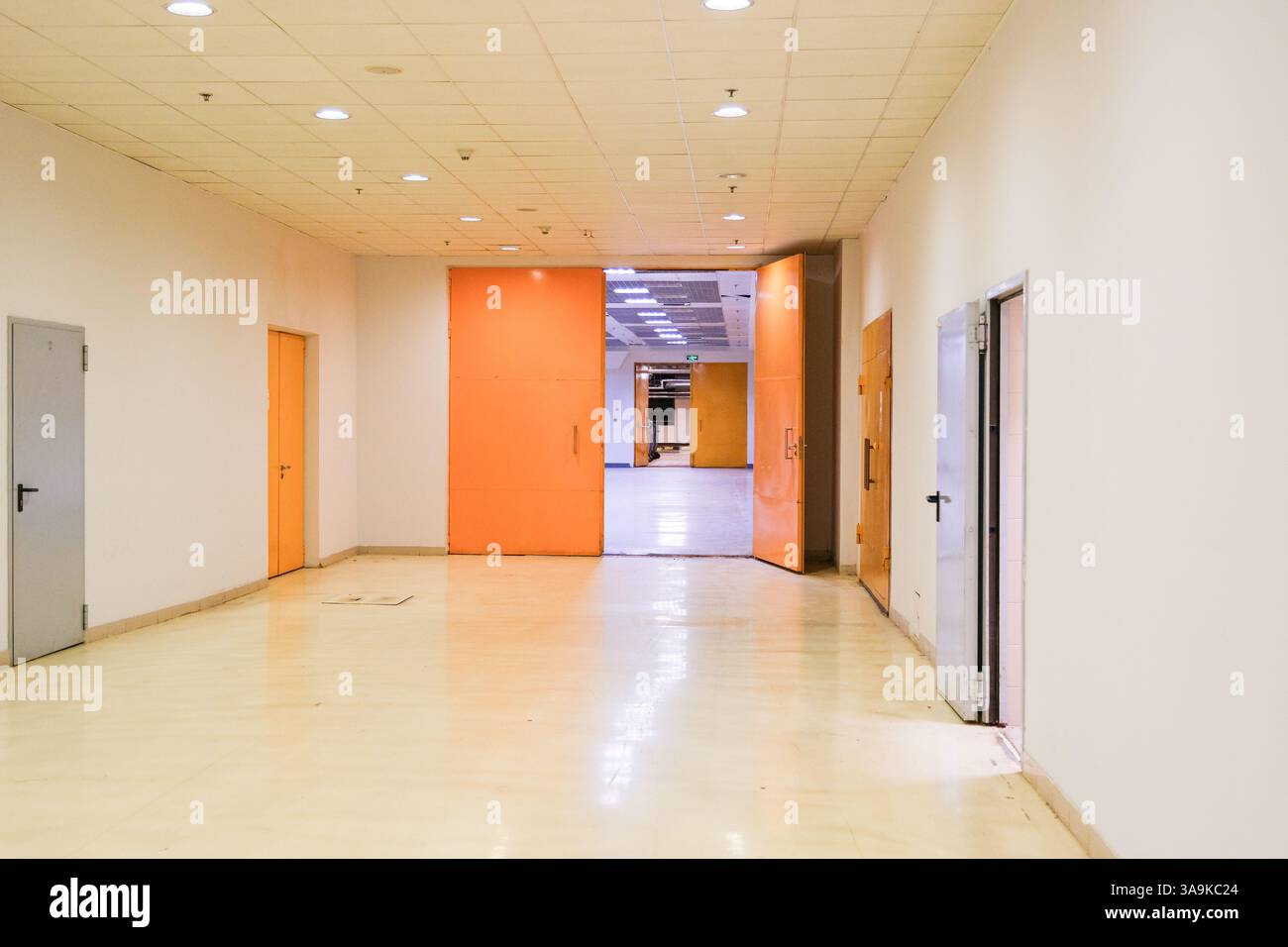 A large empty room with orange doors and a white wall. The room is ...