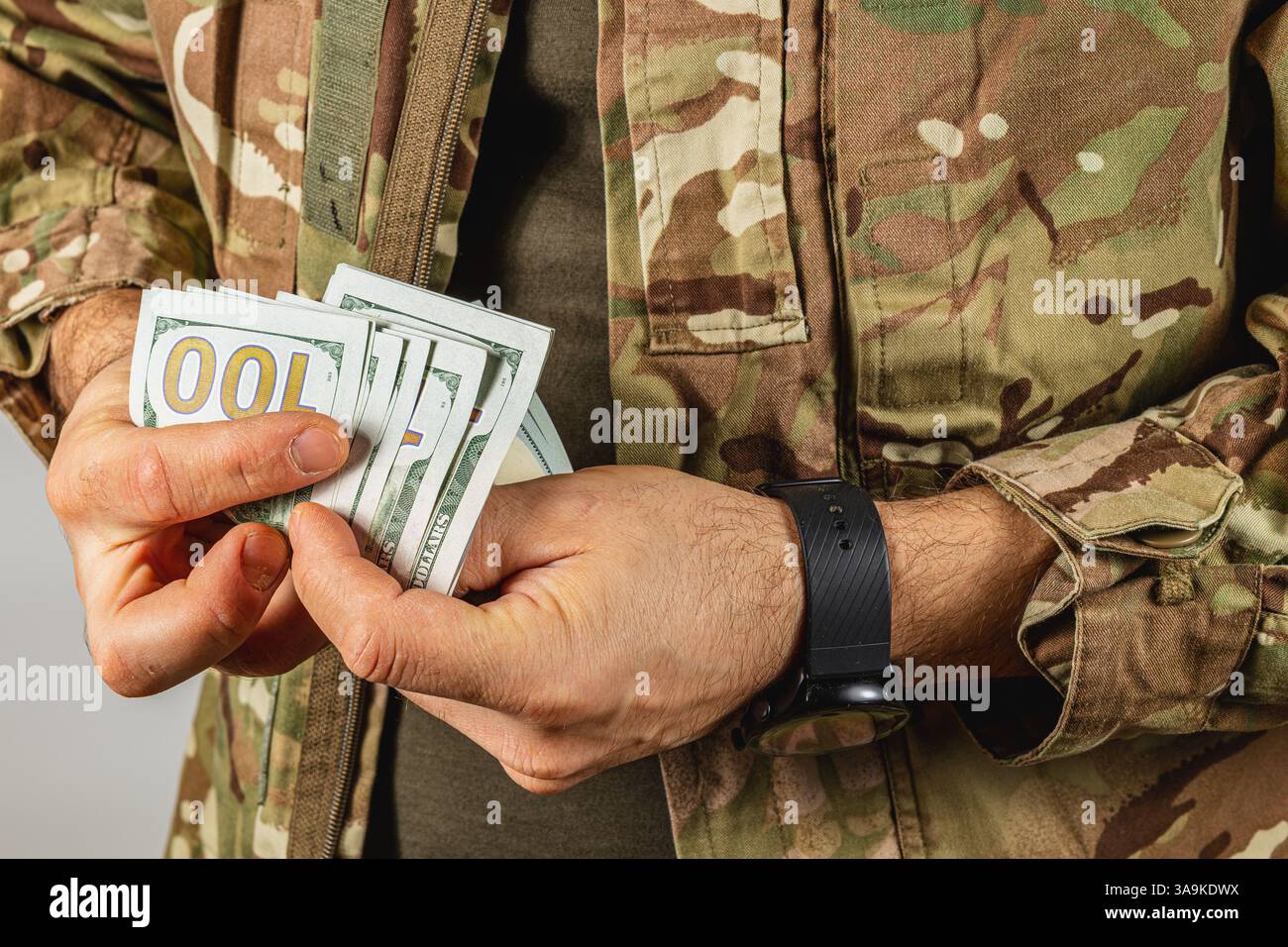 A soldier in a camouflage uniform is counting a stack of hundred-dollar ...