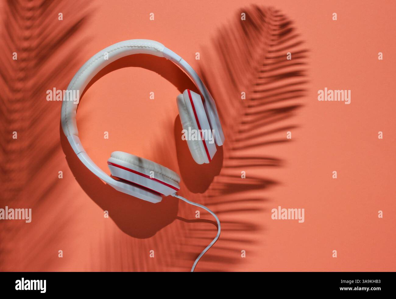 Classic white wired headphones on coral paper background with palm leaf ...