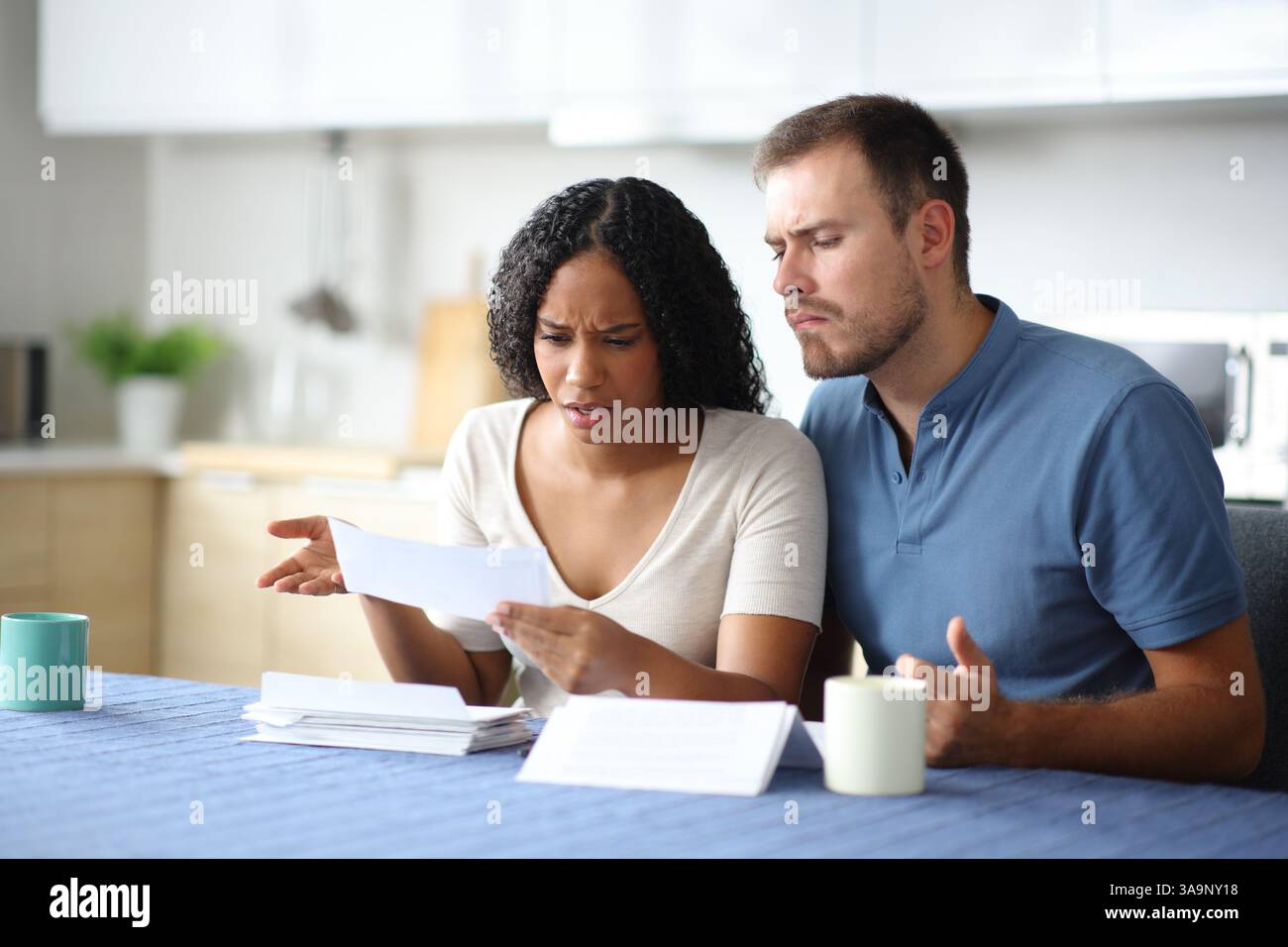 Angry interracial couple reading bank statement in the kitchen at home ...