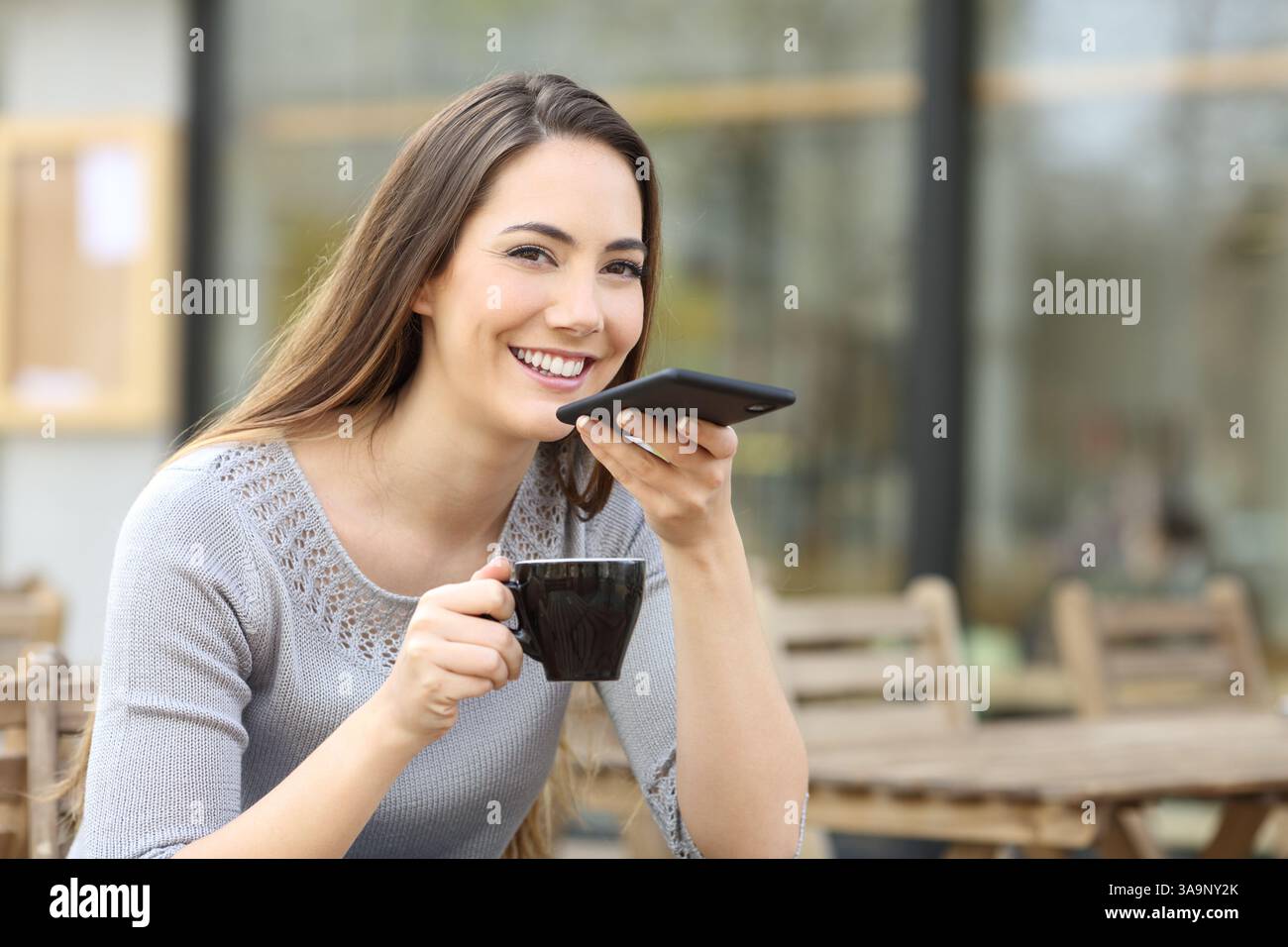 Happy woman sitting in a bar terrace dictating message on phone ...