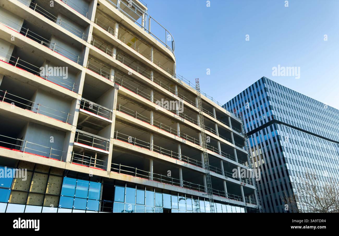 A multi-level concrete building under construction stands next to a ...