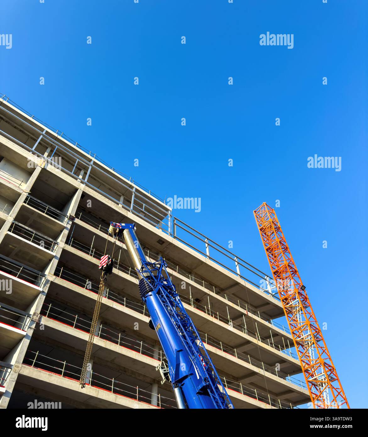 A blue hydraulic crane with chains extended operates beside an orange ...