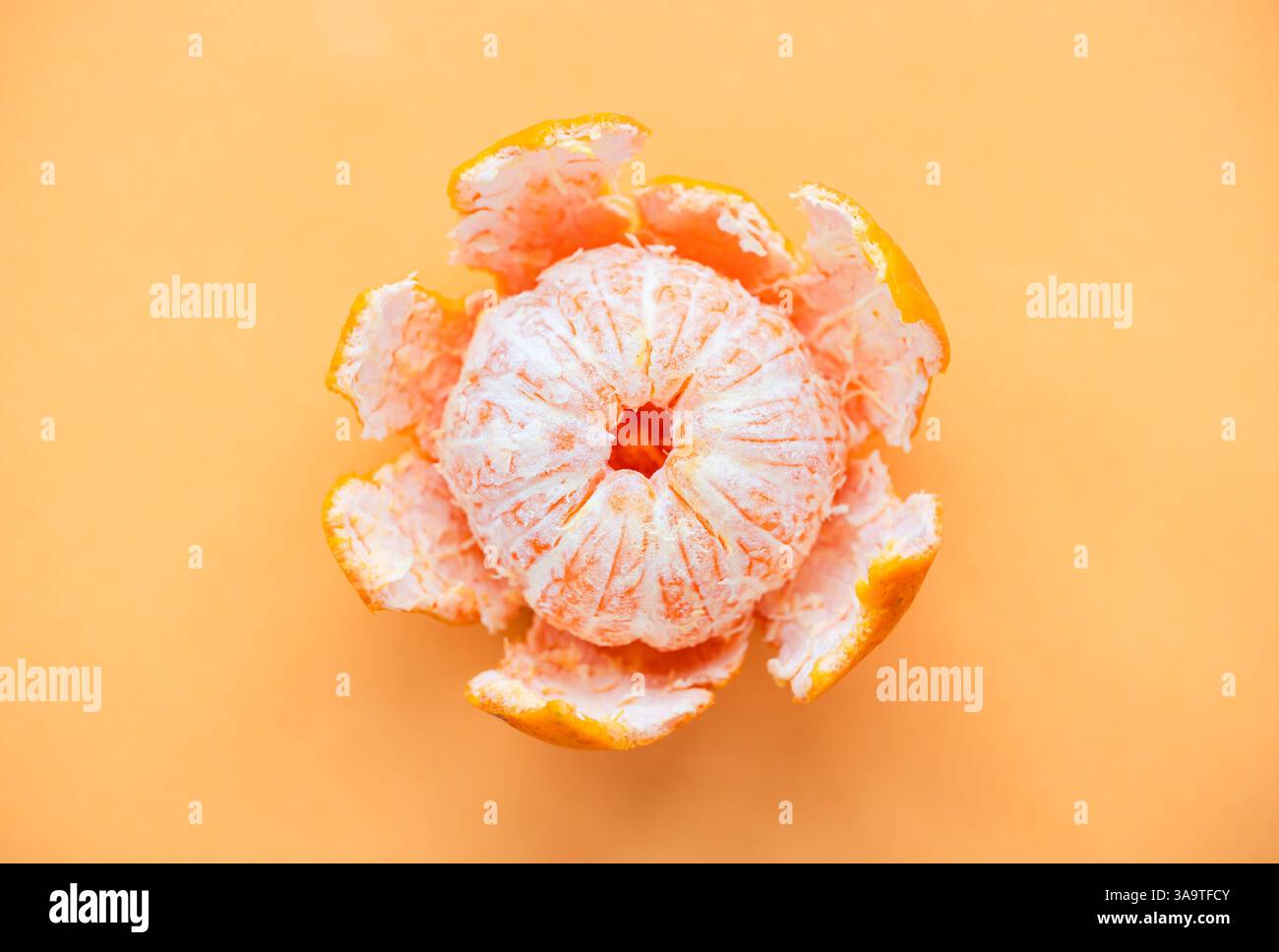 Top view of clementine with peel partially off on orange background ...
