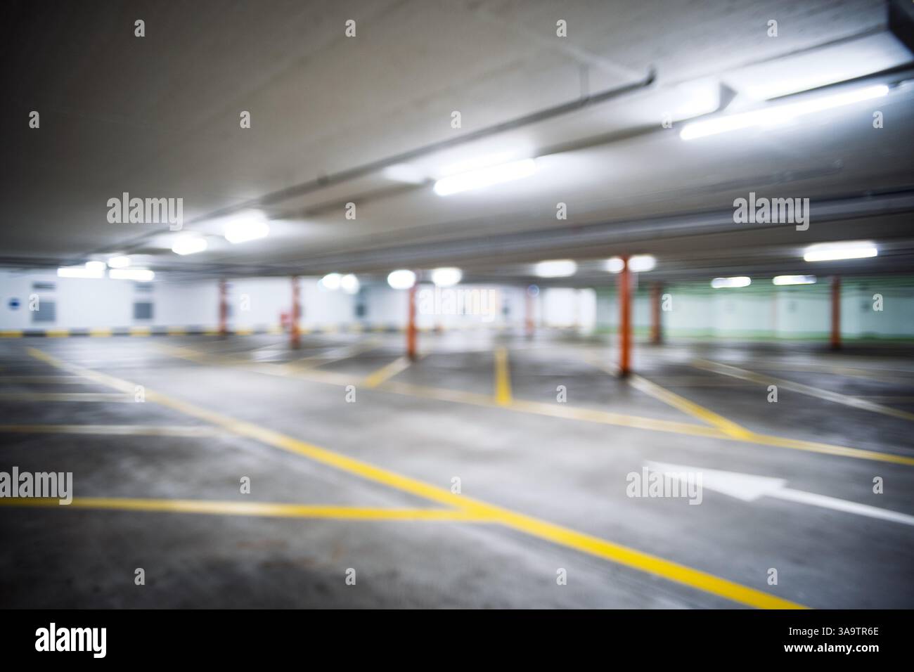 Blurred, empty, illuminated underground car parking lot. Wide angle ...