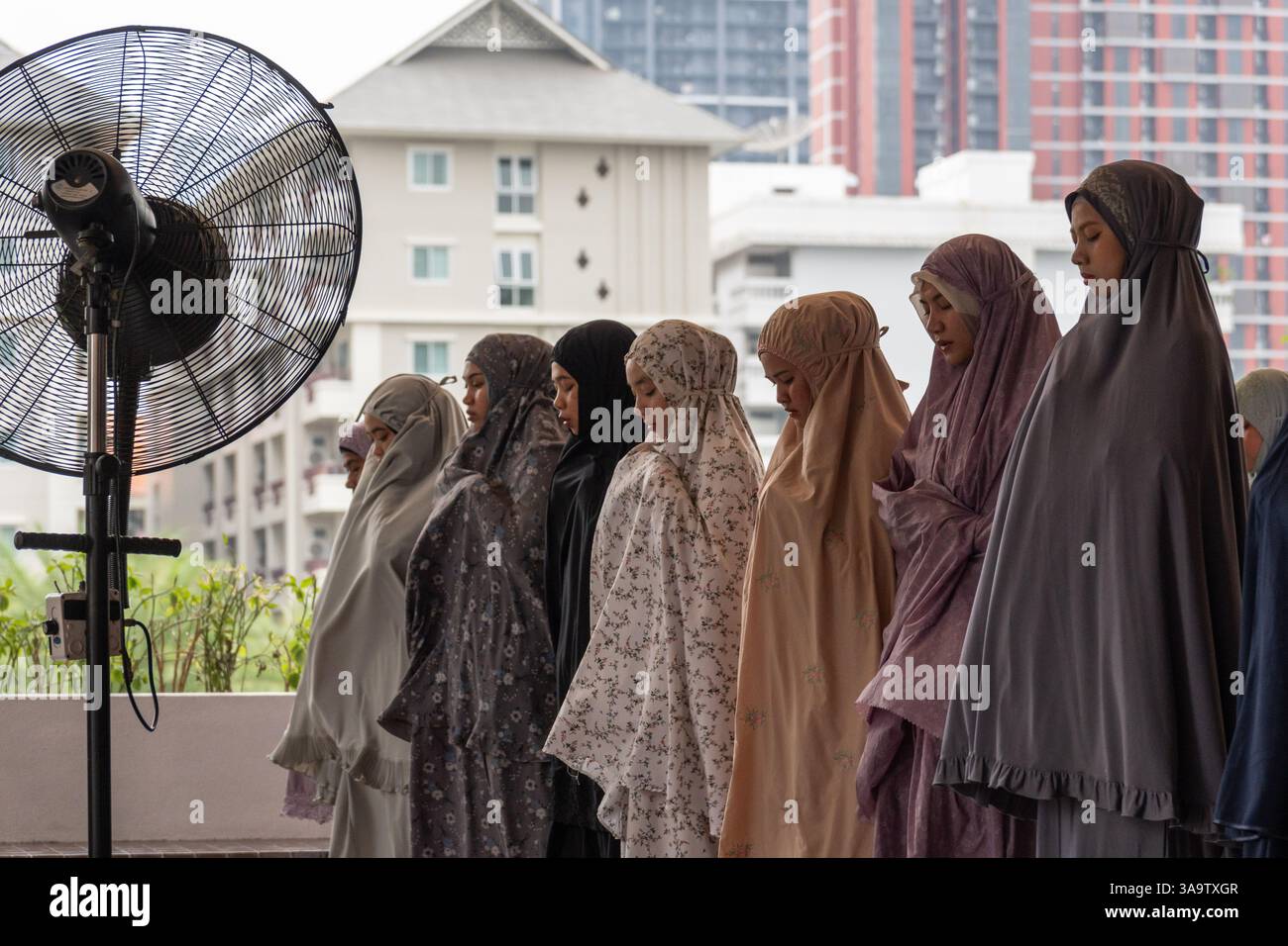 A view of Muslim women standing and praying near a fan due to the hot ...