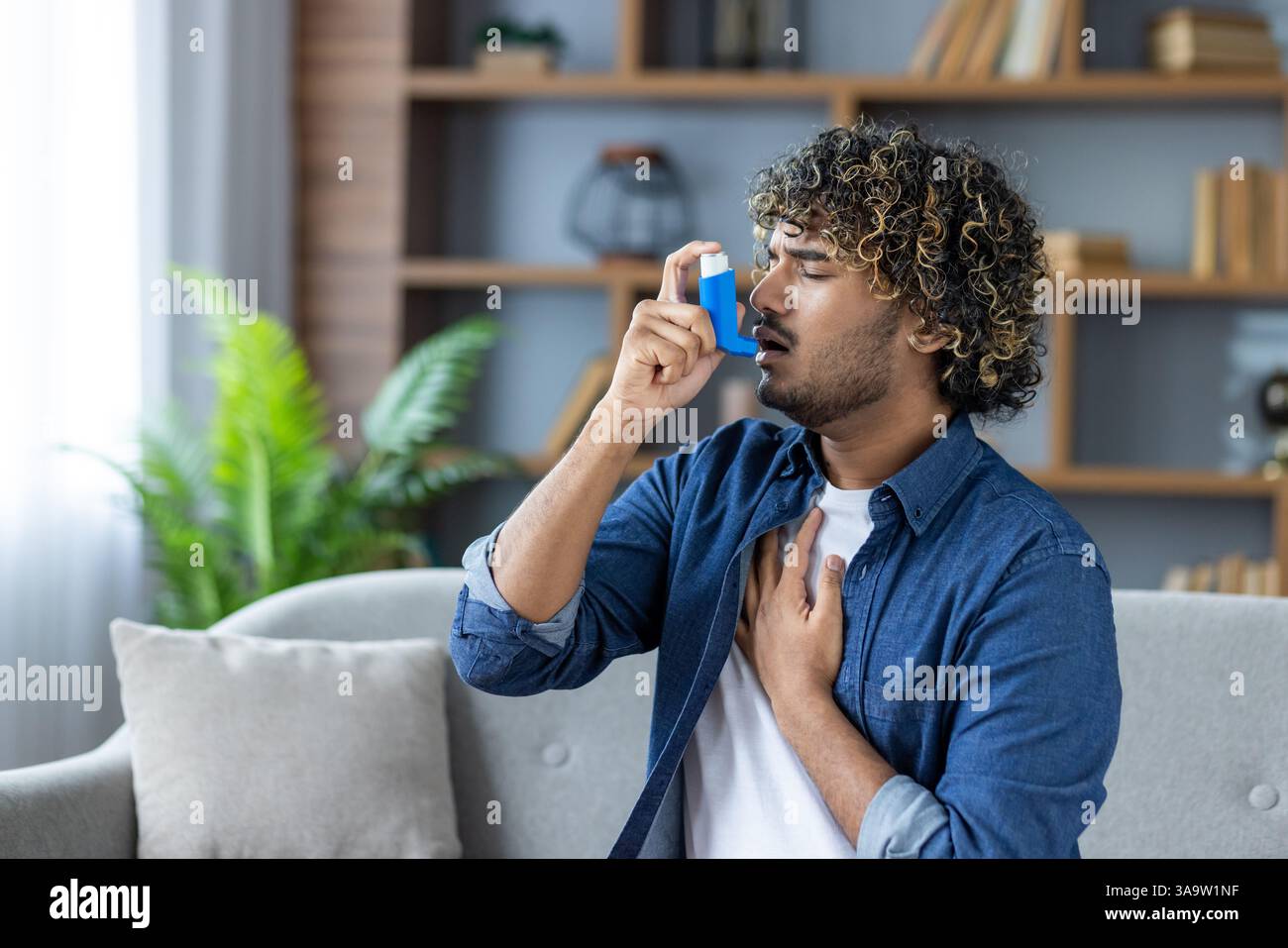 A young man with curly hair is using an inhaler for his asthma while ...