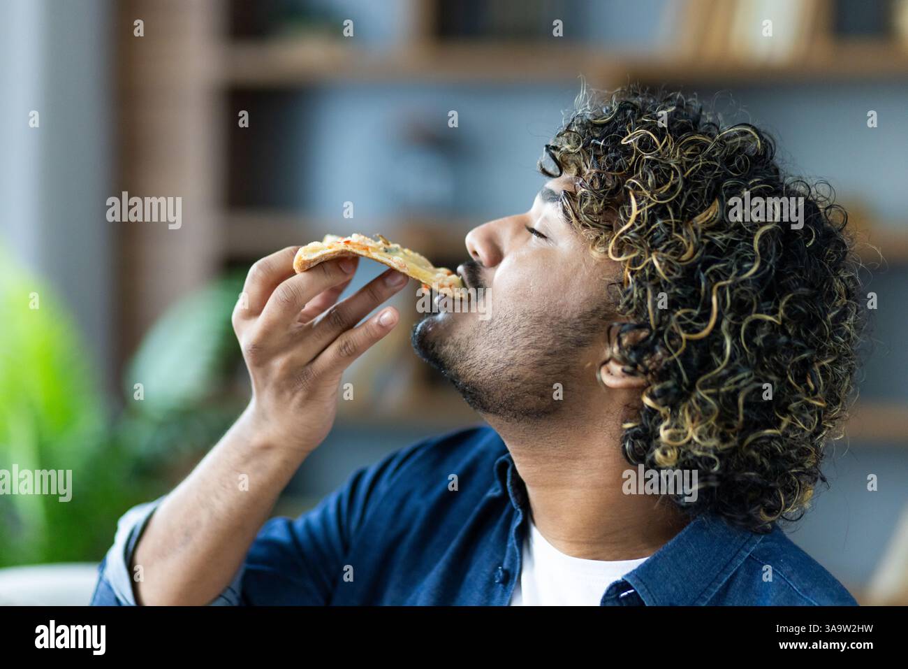 Young satisfied man at home close up eating pizza while sitting on sofa ...