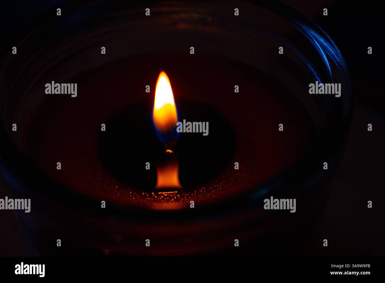 Beautiful burning candle with the flame reflection on the melted wax ...
