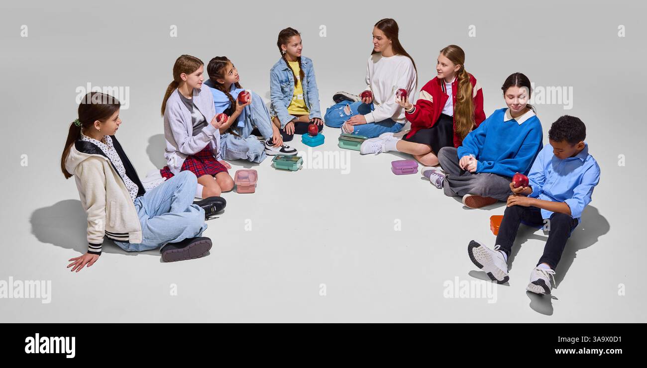Group of students sit in circle, each holding red apple with lunchboxes ...