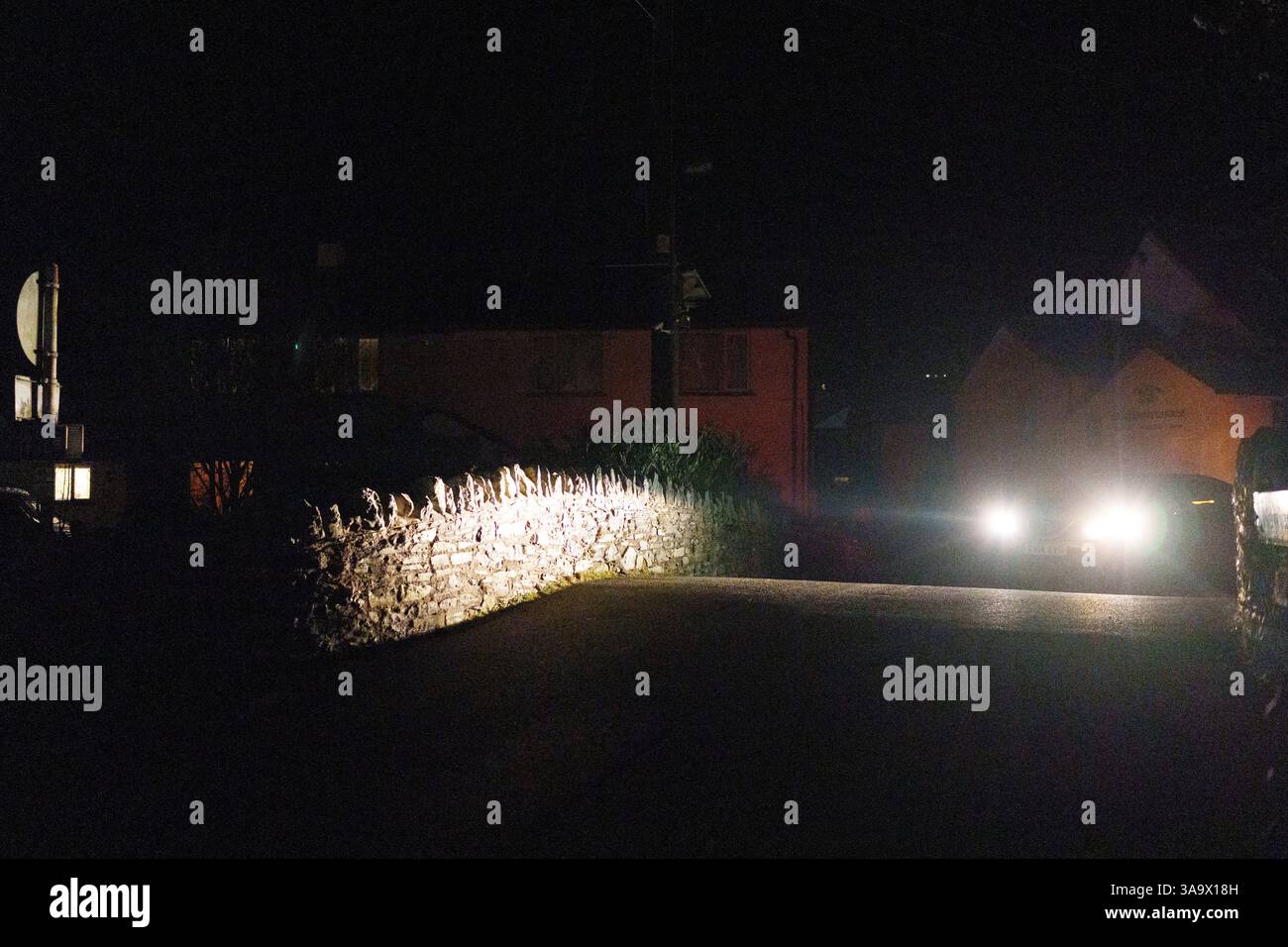 The bright glare of a car's headlights which illuminate the stone wall ...