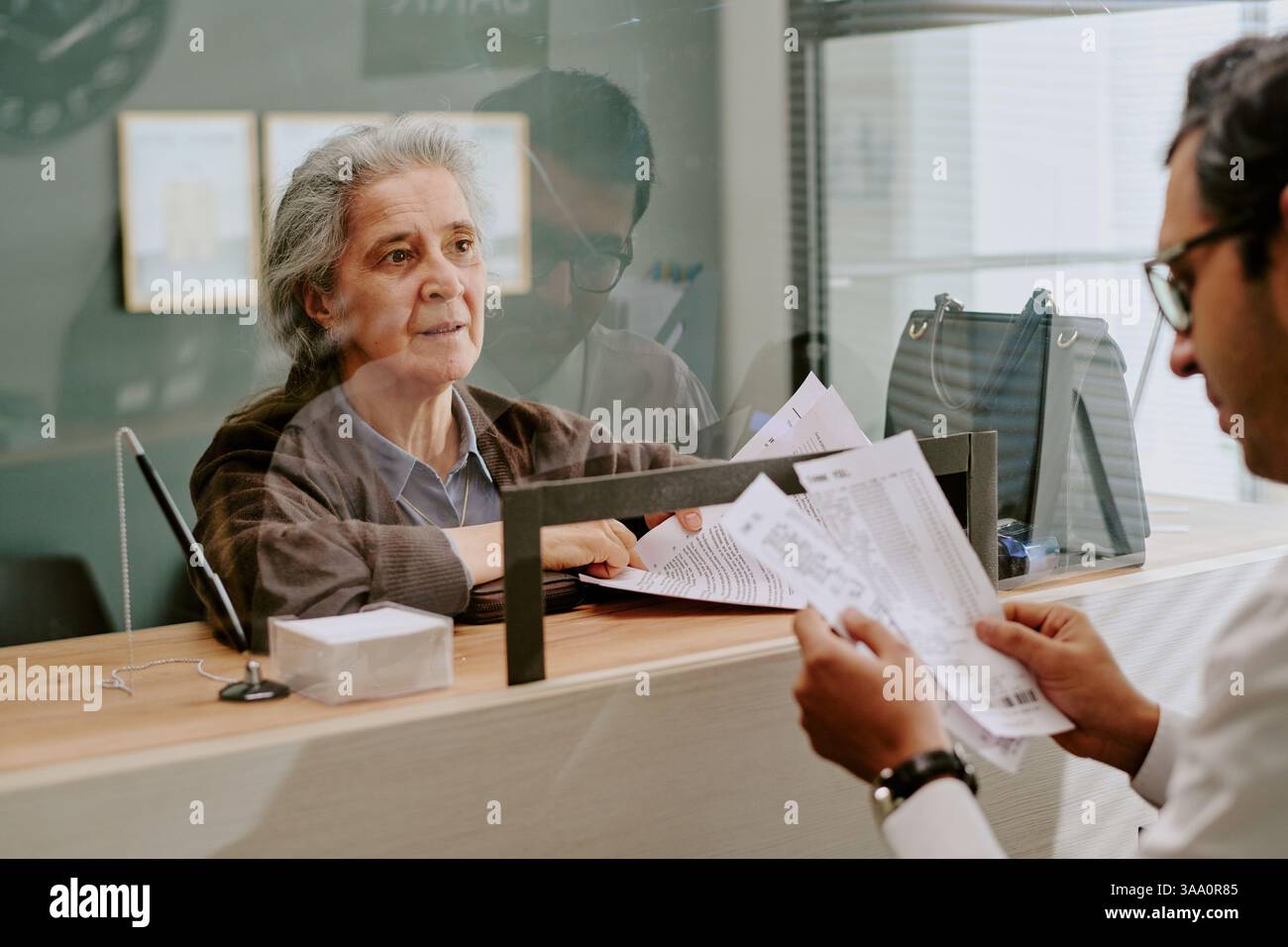 Senior woman behind reception desk assisting a man with important ...
