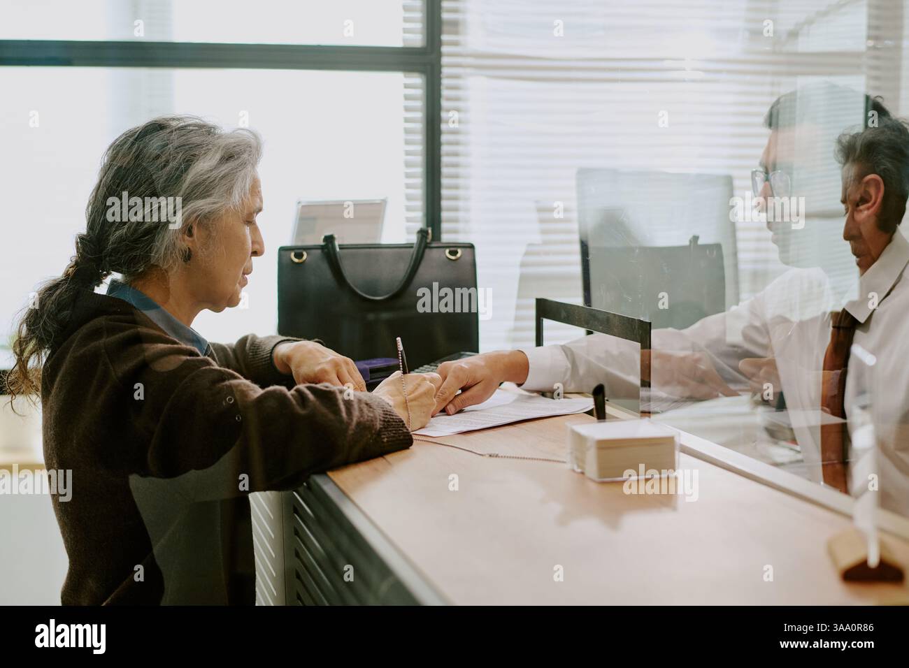 Elderly woman discussing and signing documents at modern office counter ...