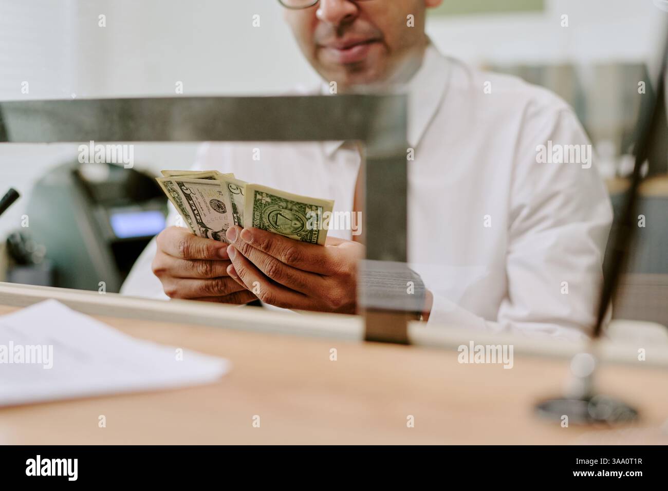 Bank employee counting cash bills at counter behind transparent glass ...