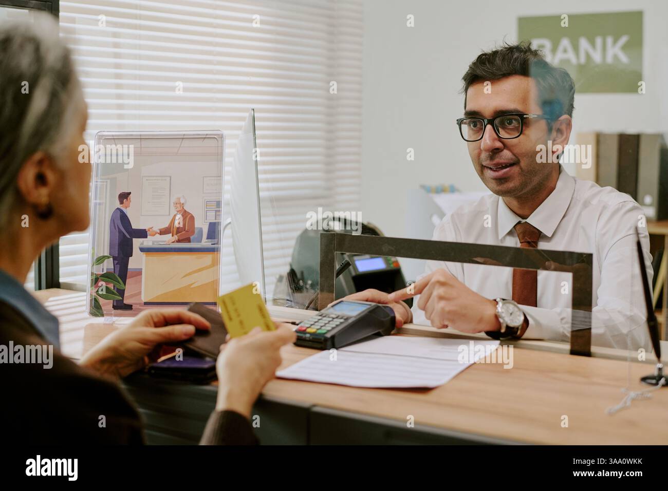 Bank teller wearing glasses professionally assisting senior customer ...