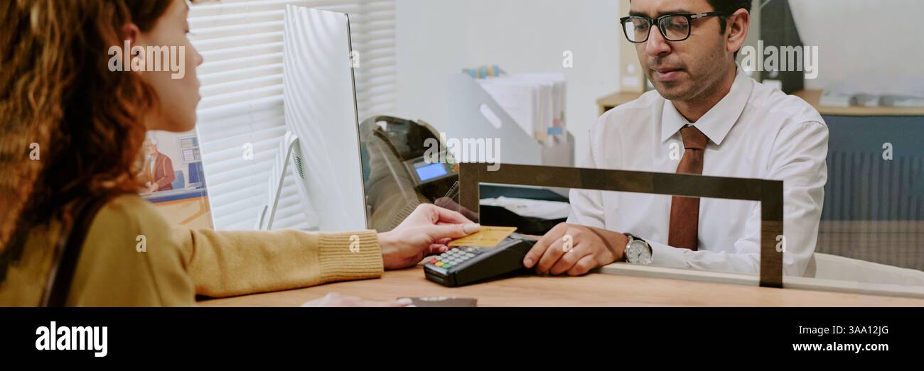 Customer making payment at bank counter using card reader with teller ...