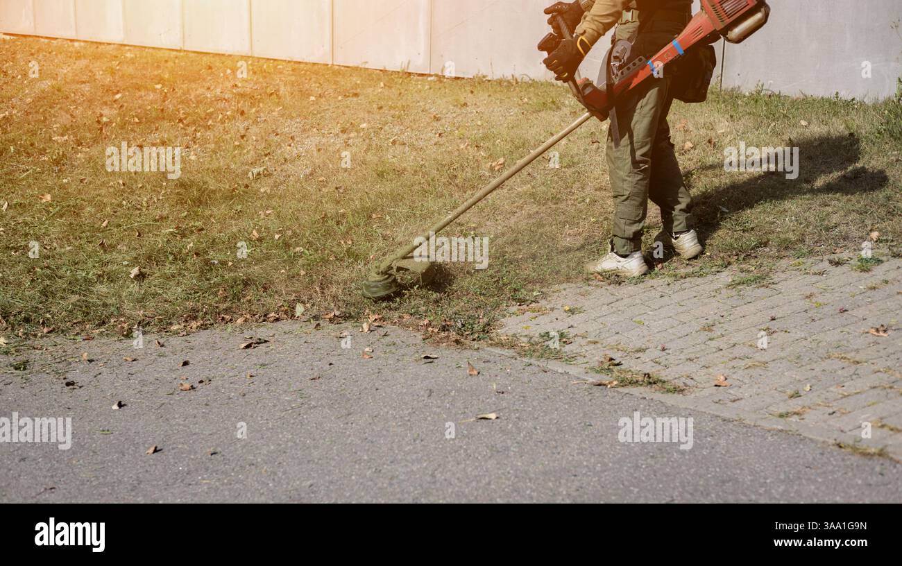 Professional gardener mowing tall grass with lawn trimmer in city park ...