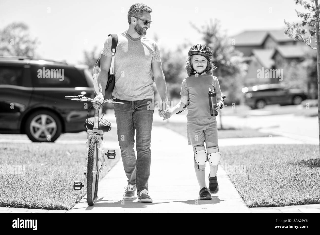 supportive dad guiding his son first bike ride. dad and son enjoying ...