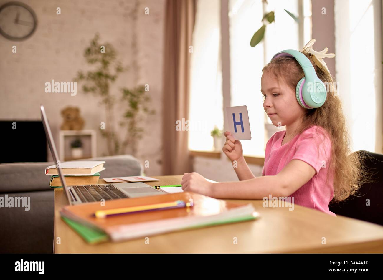 Focused girl, primary school student showing flashcard with letter H ...