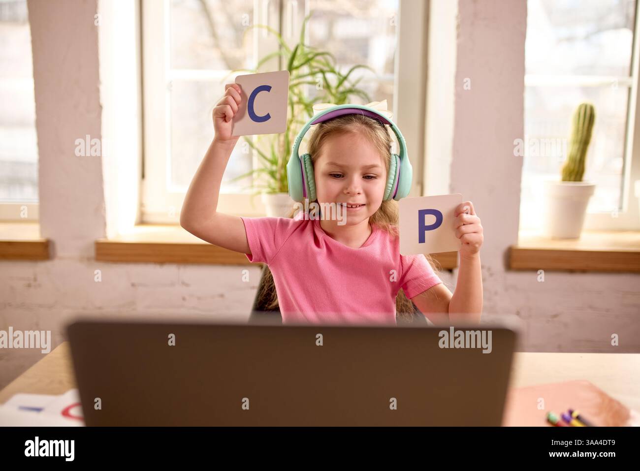 Smiling schoolgirl showing flashcards with letters C and P to laptop ...