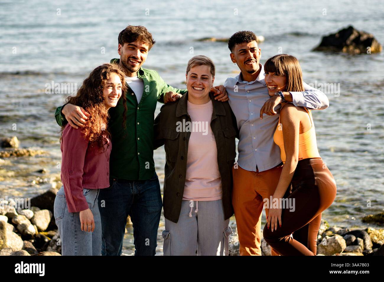 A diverse group of friends smiling and bonding by the seaside on a ...