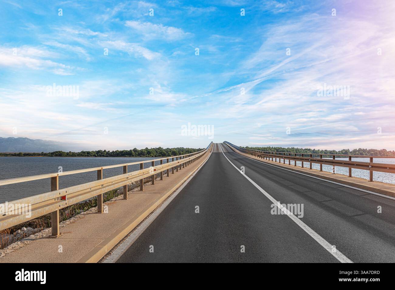 A long, straight bridge stretches over a body of water under a bright ...