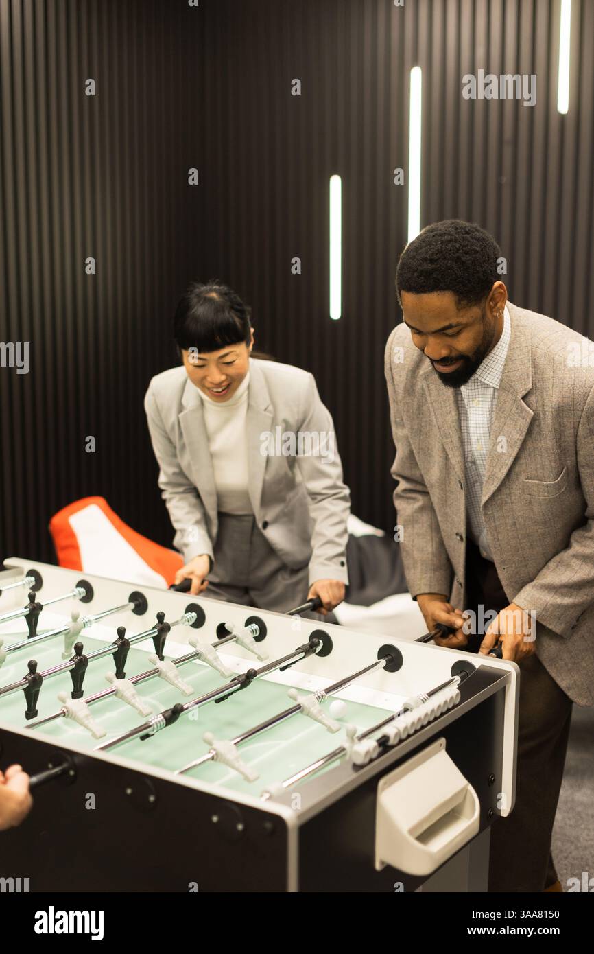 Two colleagues enjoy a lively match of foosball in a contemporary ...
