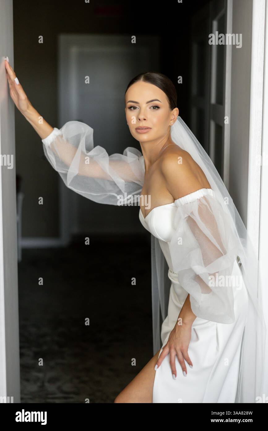 Elegant bride wearing white wedding dress and veil entering room, looking back over her shoulder ...