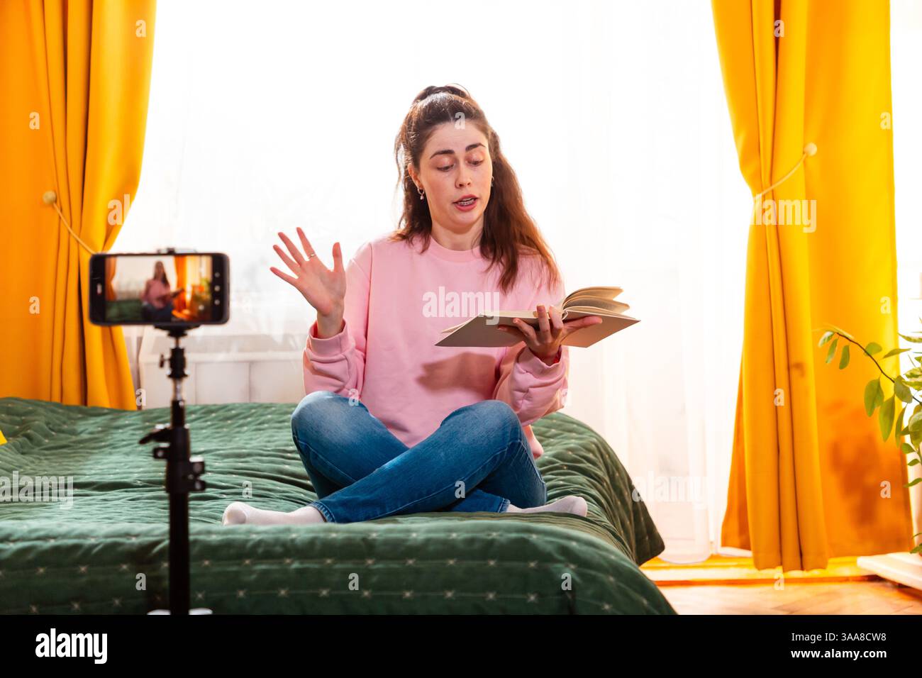 Young Caucasian woman filming herself at home while sitting on a bed ...