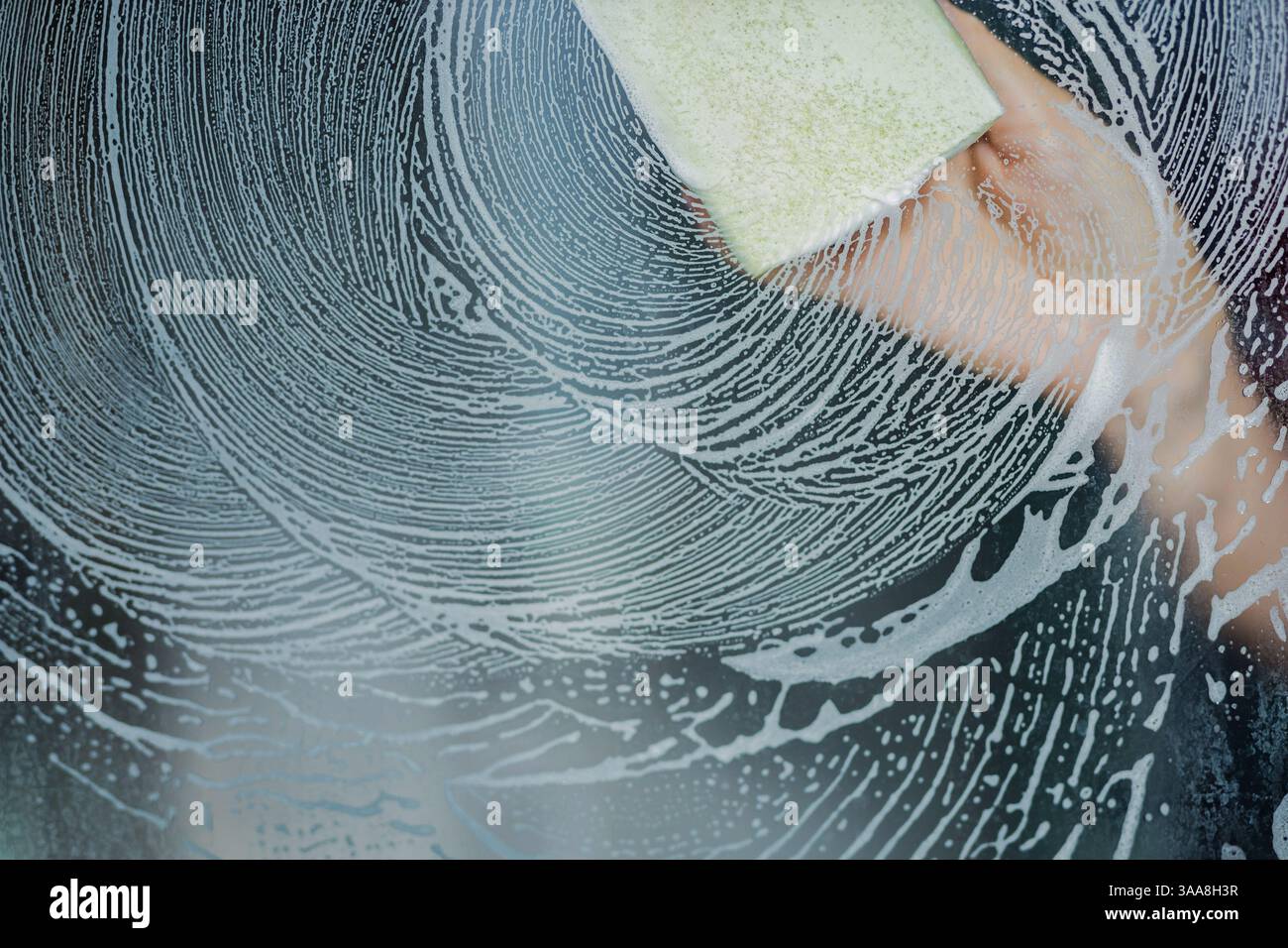 Сlose up of glass surface covered in soapy foam with sponge wiping it ...