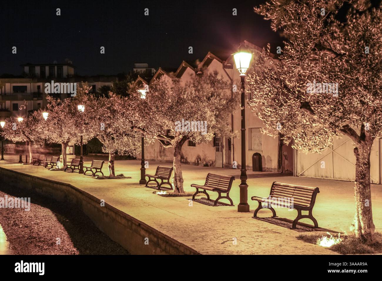 A row of benches are lined up along a sidewalk. The benches are lit up ...