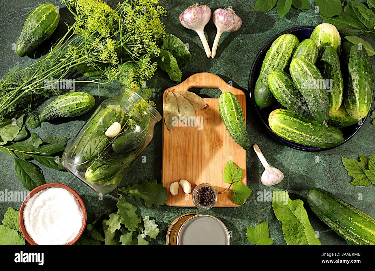 Fresh cucumbers in a jar, spices, garlic and leaves on a concrete ...
