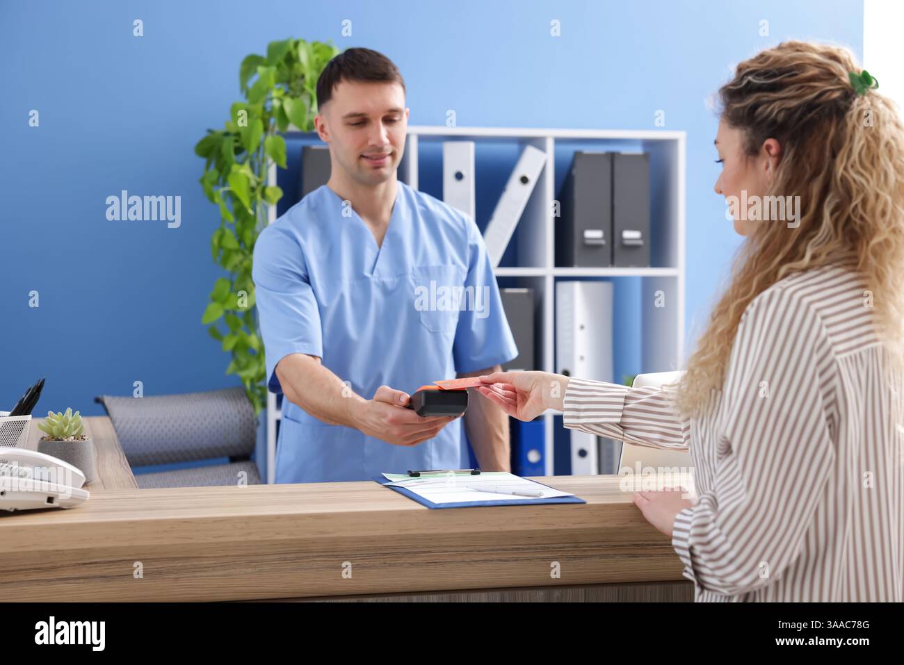 Smiling receptionist taking payment from patient via terminal at ...