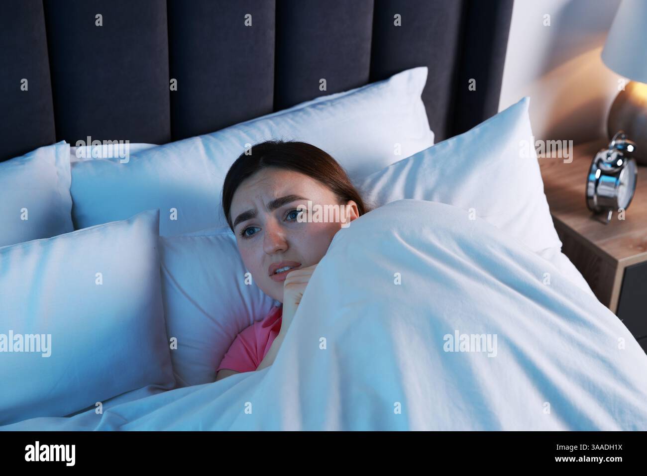 Fear of darkness. Scared young woman lying on bed in room at night ...