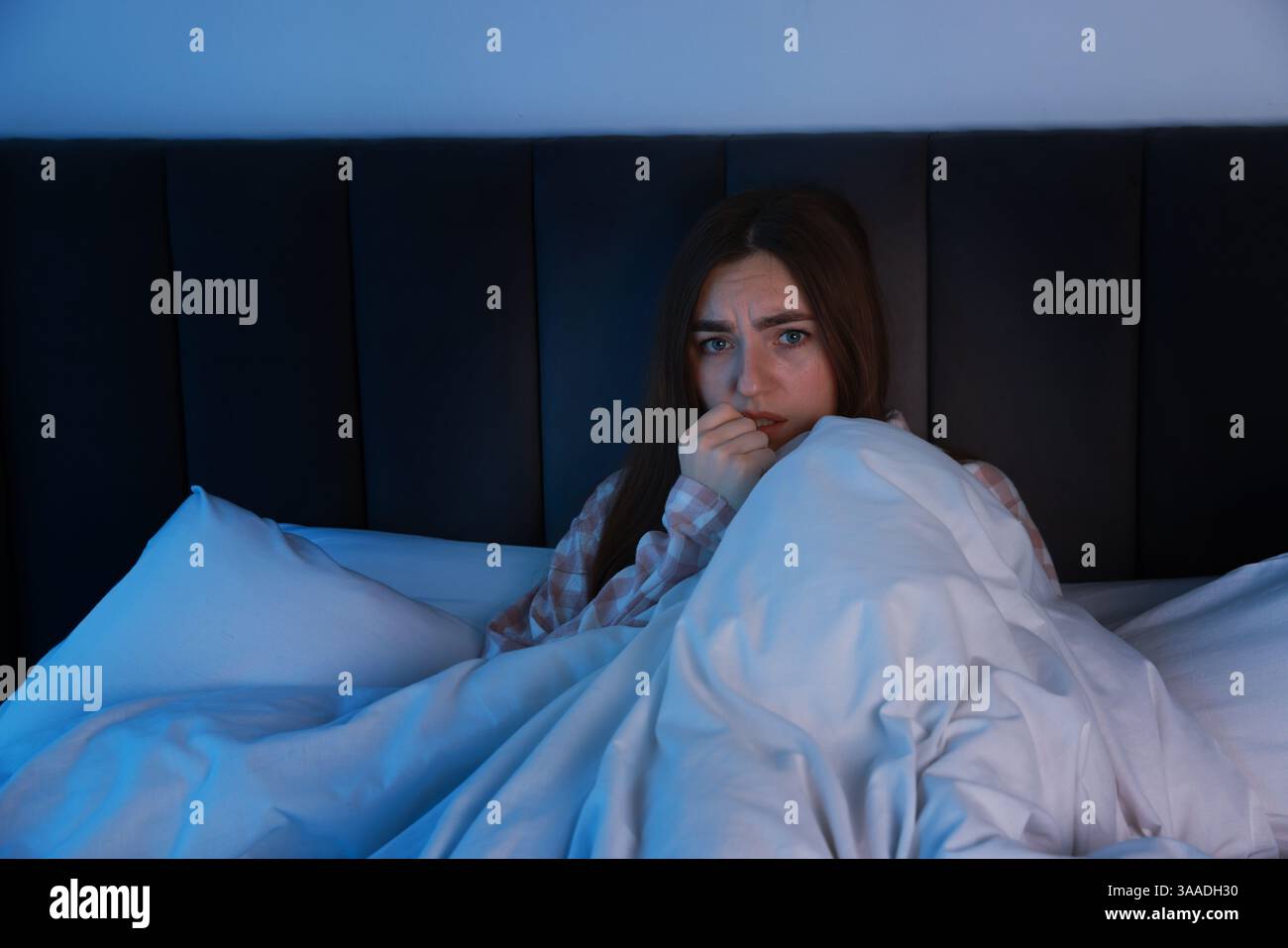 Fear of darkness. Scared young woman lying on bed in room at night ...