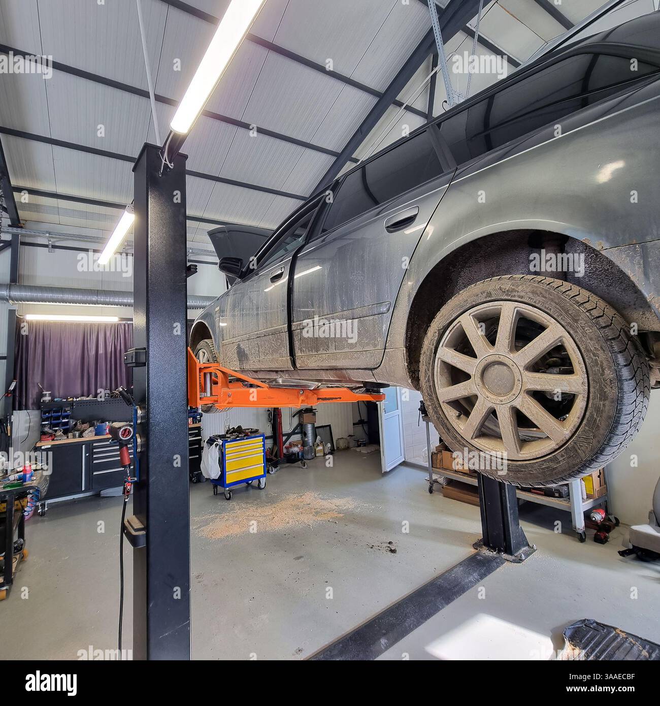A dark colored station wagon with its hood open is lifted on a ...