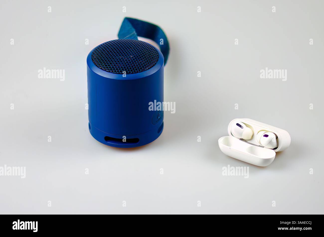 Compact blue speaker with mesh grille and strap next to white wireless ...
