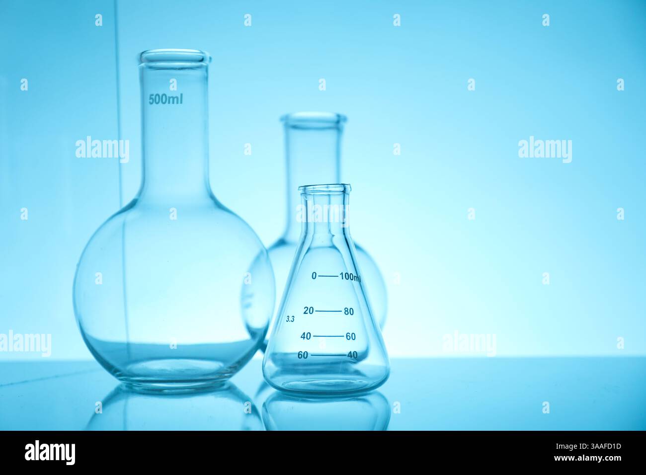 Empty flasks on mirror surface against light blue background, space for ...