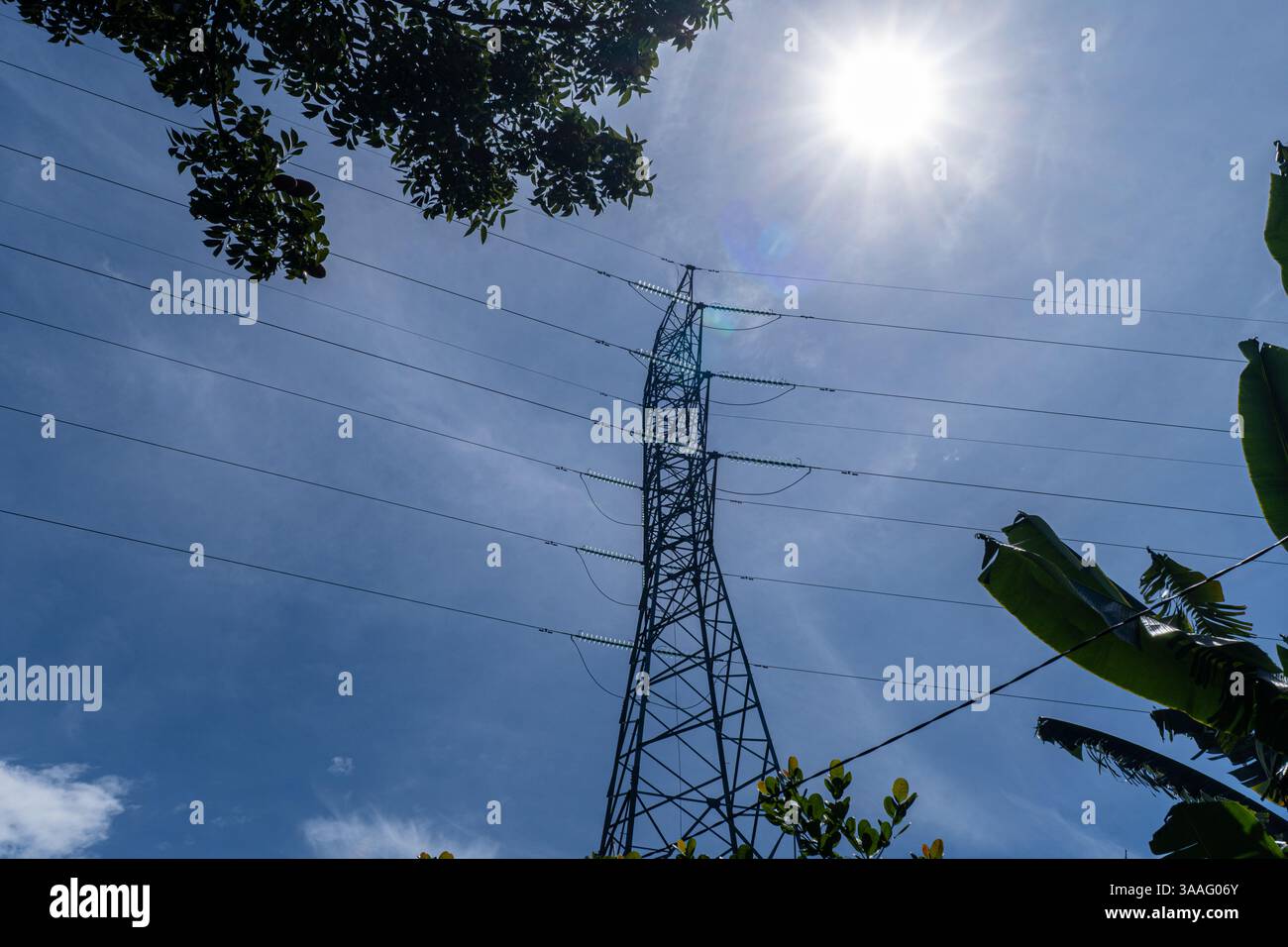 A towering electricity pylon with power lines stretching across a clear blue sky, illuminated by ...